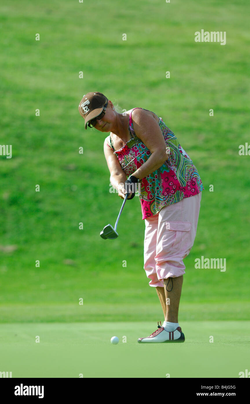 A senior woman golf player driving a put on the green golf course ...