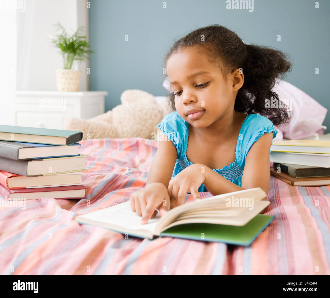 Mixed race girl reading book in bedroom Stock Photo - Alamy