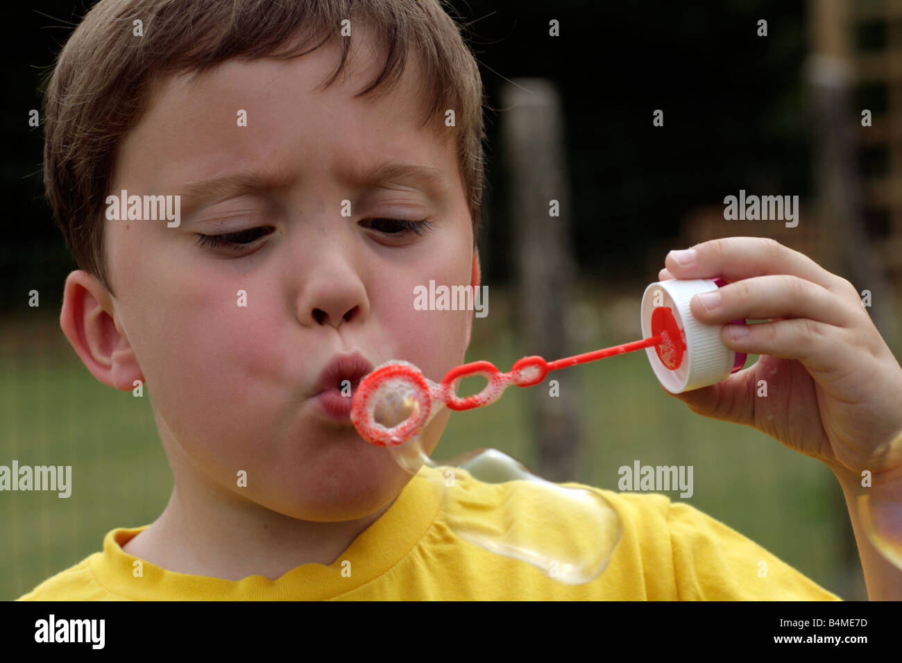 seven-year-old boy blowing bubbles, using a bubble wand and a bottle of ...