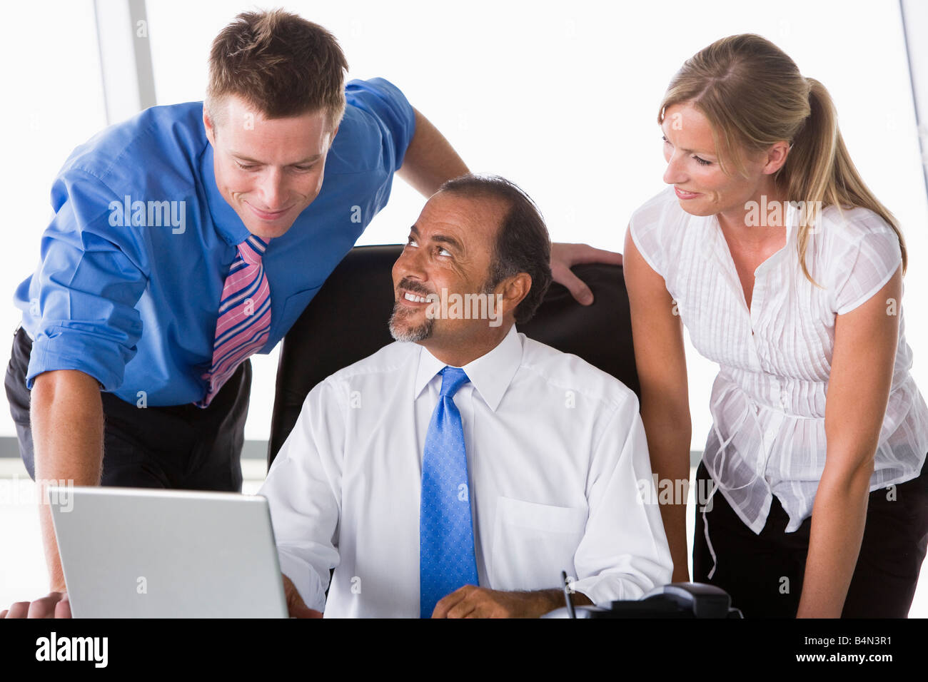 Three businesspeople in office with laptop talking and smiling (high ...