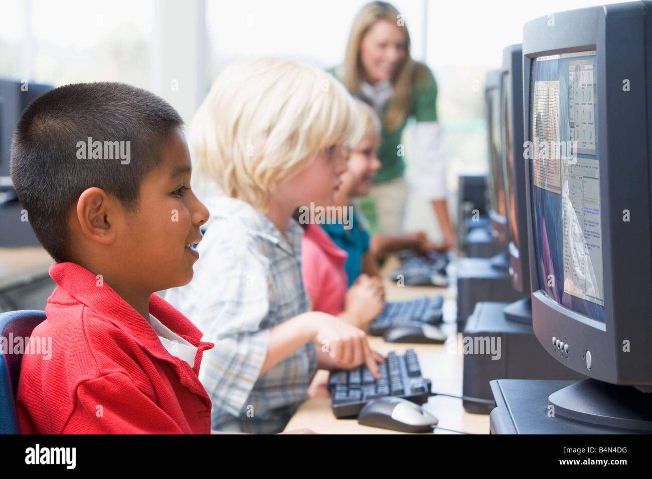 Four children at computer terminals with teacher in background (depth ...