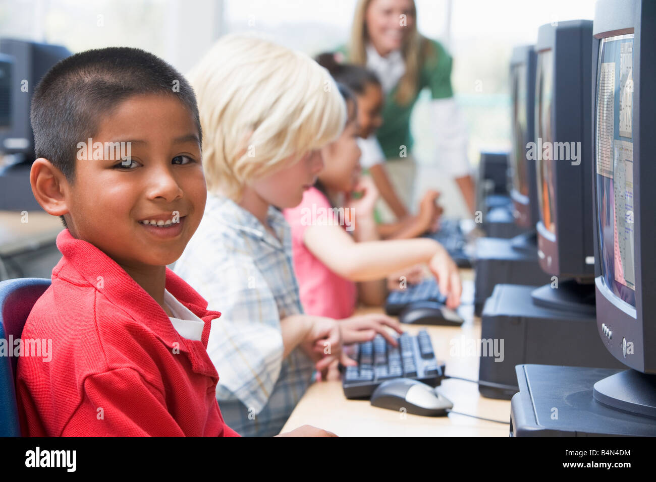 Four children at computer terminals with teacher in background (depth ...