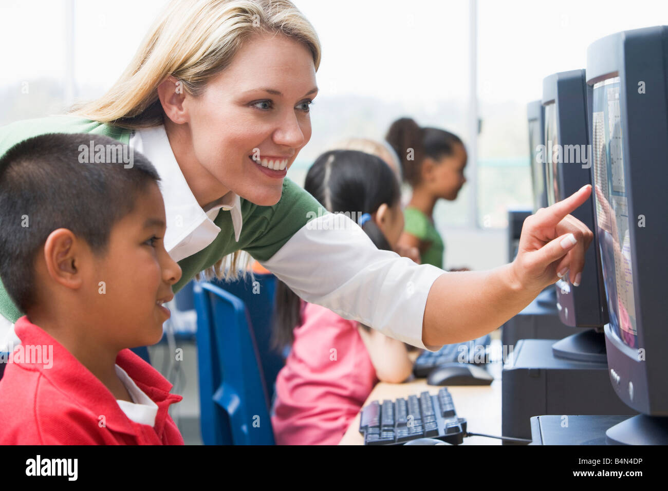 Teacher helping student at computer terminal with students in ...