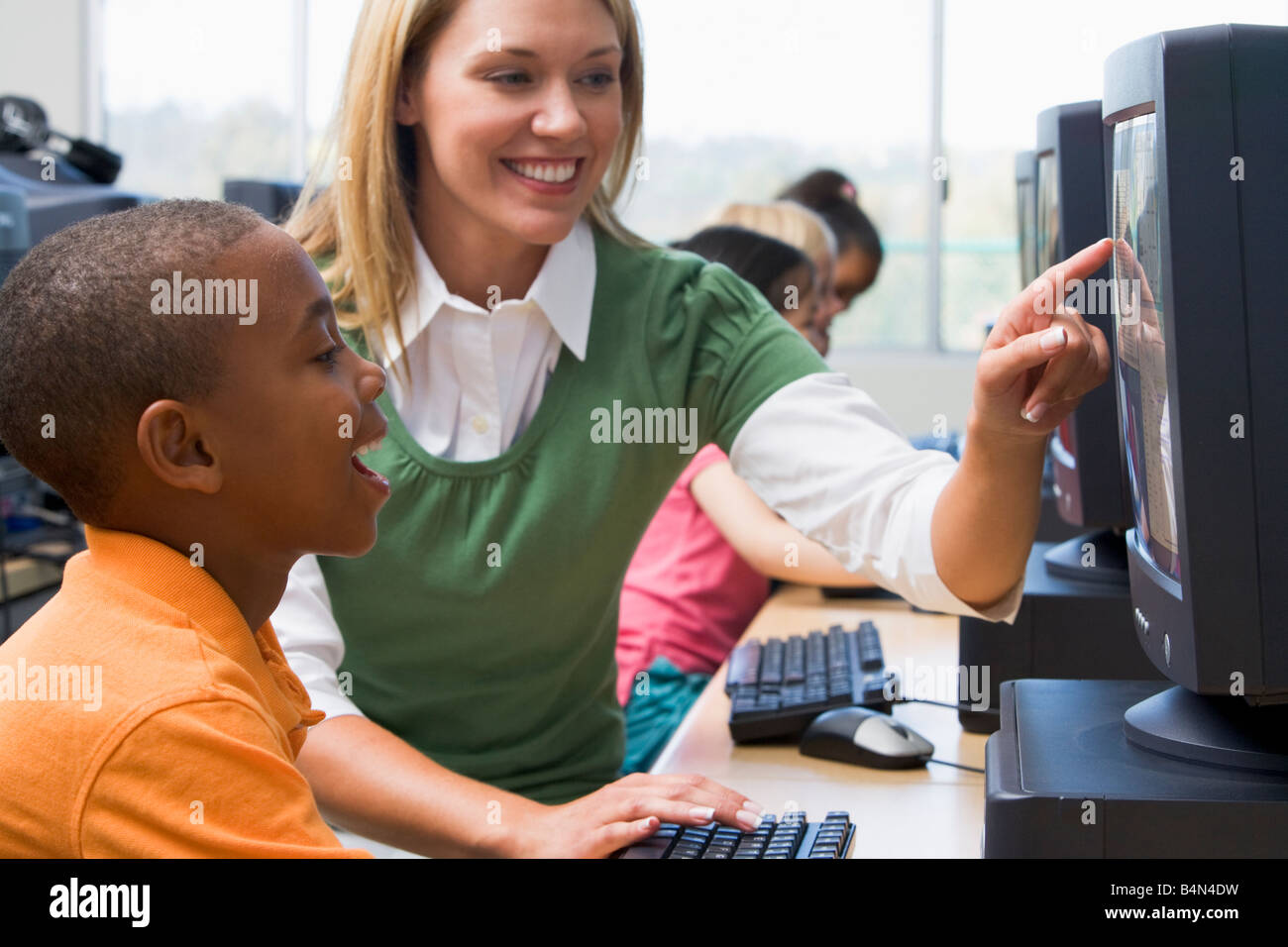 Teacher helping student at computer terminal with students in ...