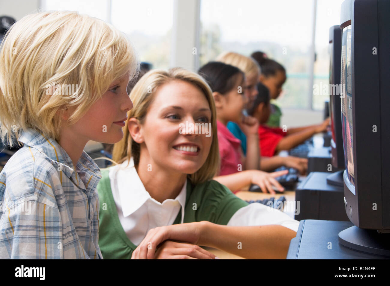 Teacher helping student at computer terminal with students in ...