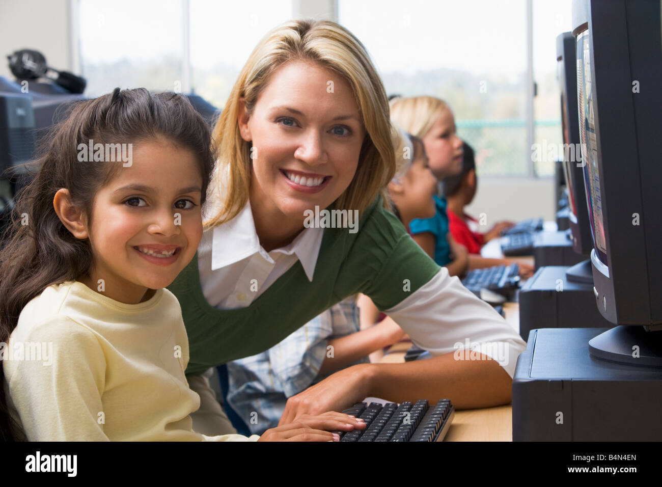 Teacher helping student at computer terminal with students in ...