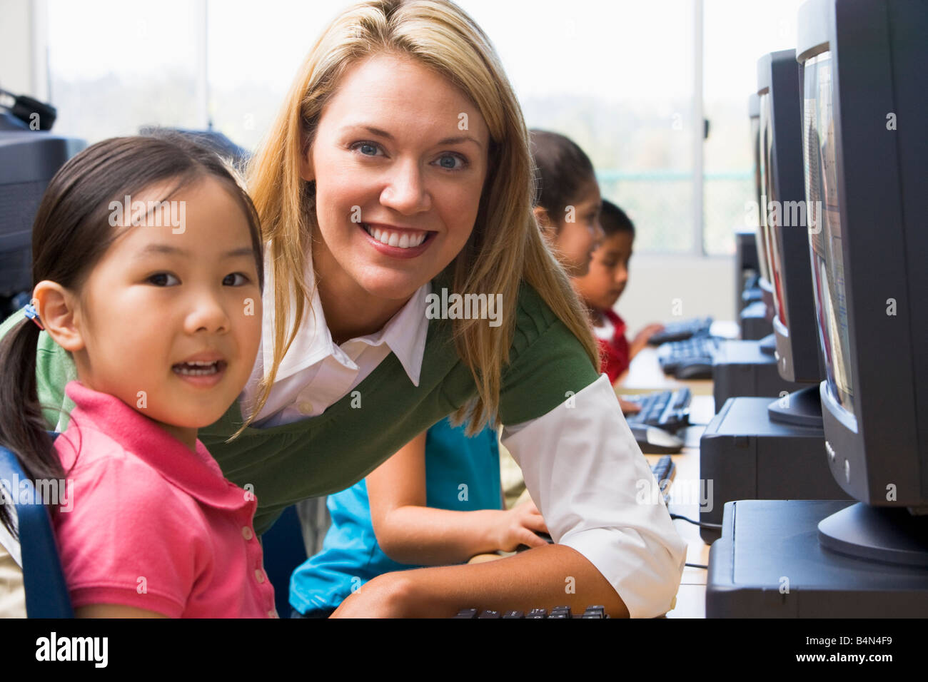 Teacher helping student at computer terminal with students in ...