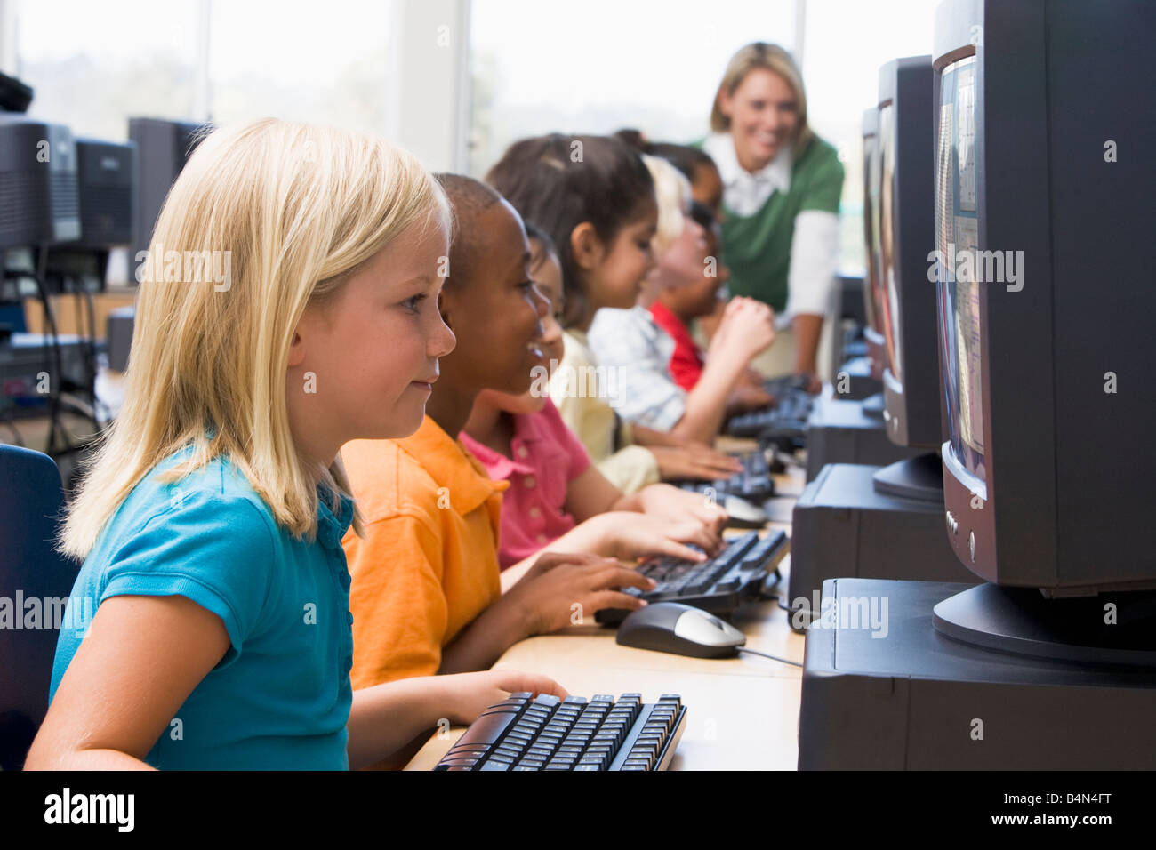 Children at computer terminals with teacher in background (depth of ...