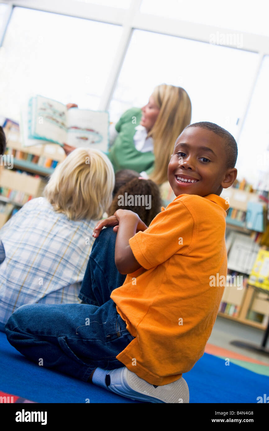 Student in class looking at camera with teacher reading in background ...