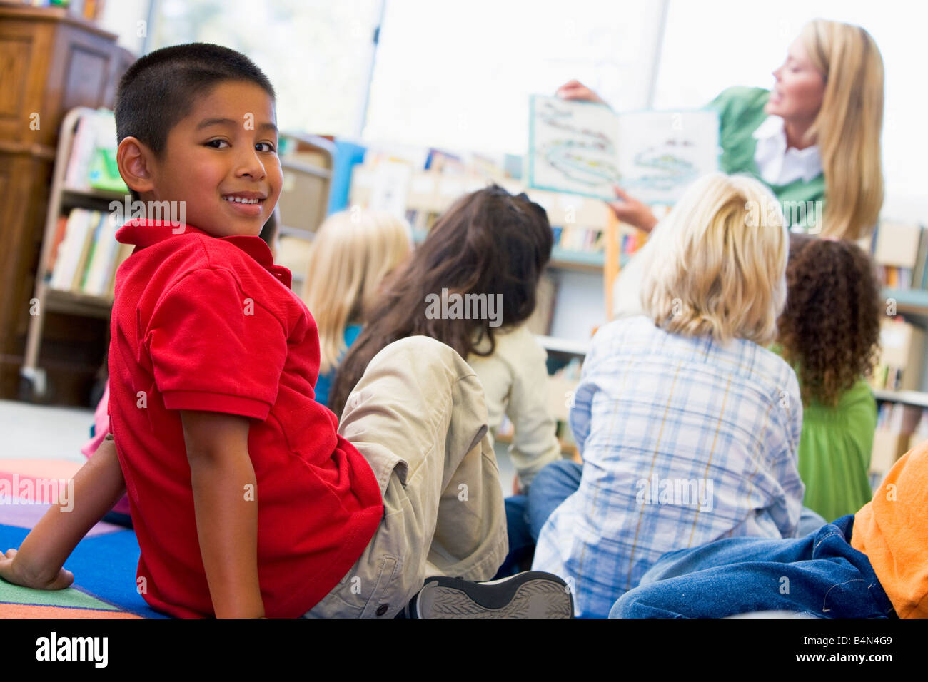 Student in class looking at camera with teacher reading in background ...