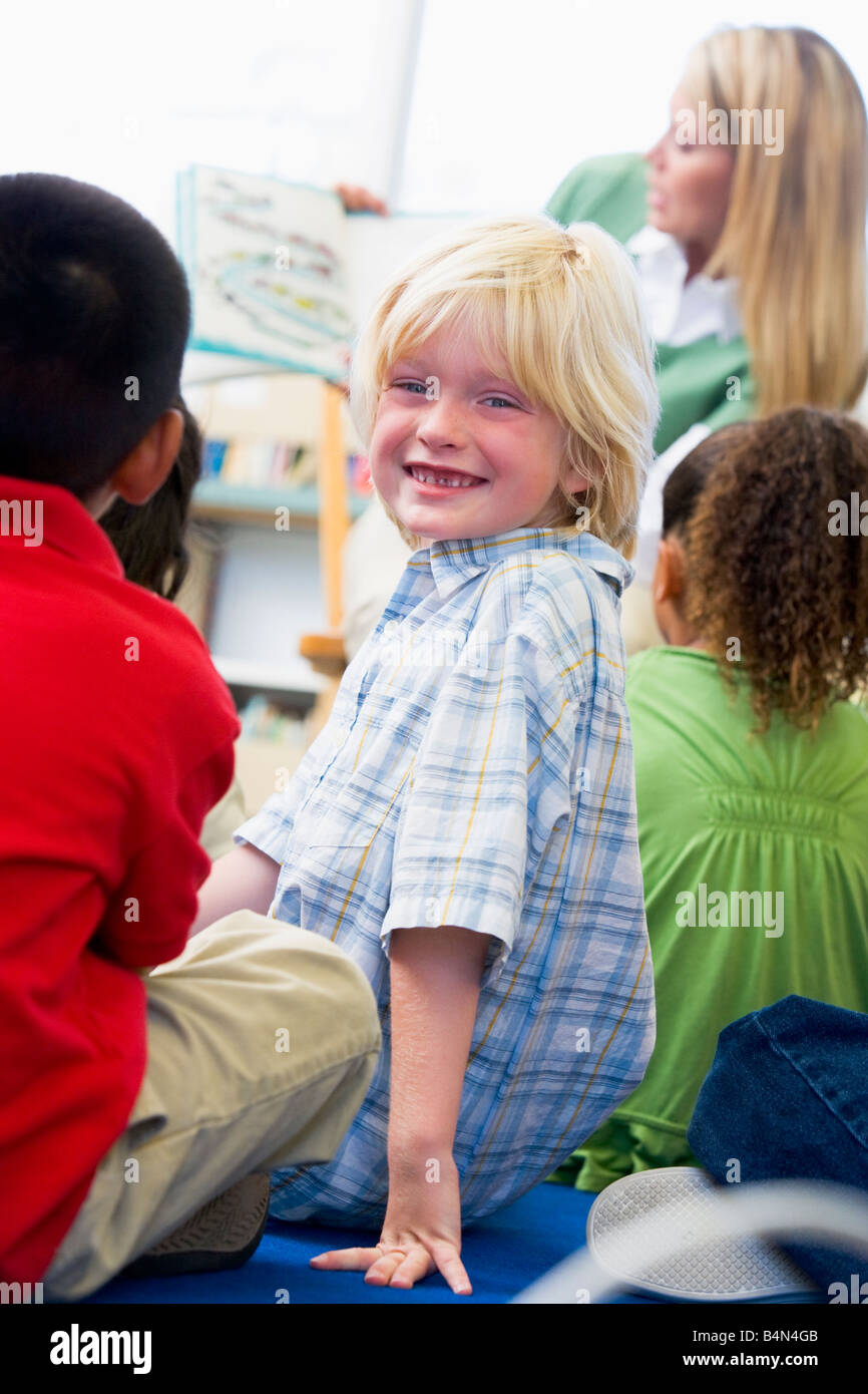 Student in class looking at camera with teacher reading in background ...