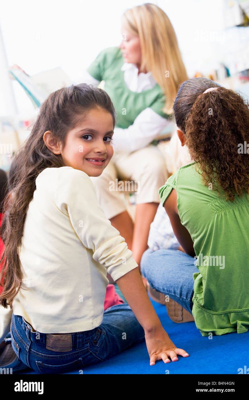 Student in class looking at camera with teacher reading in background ...