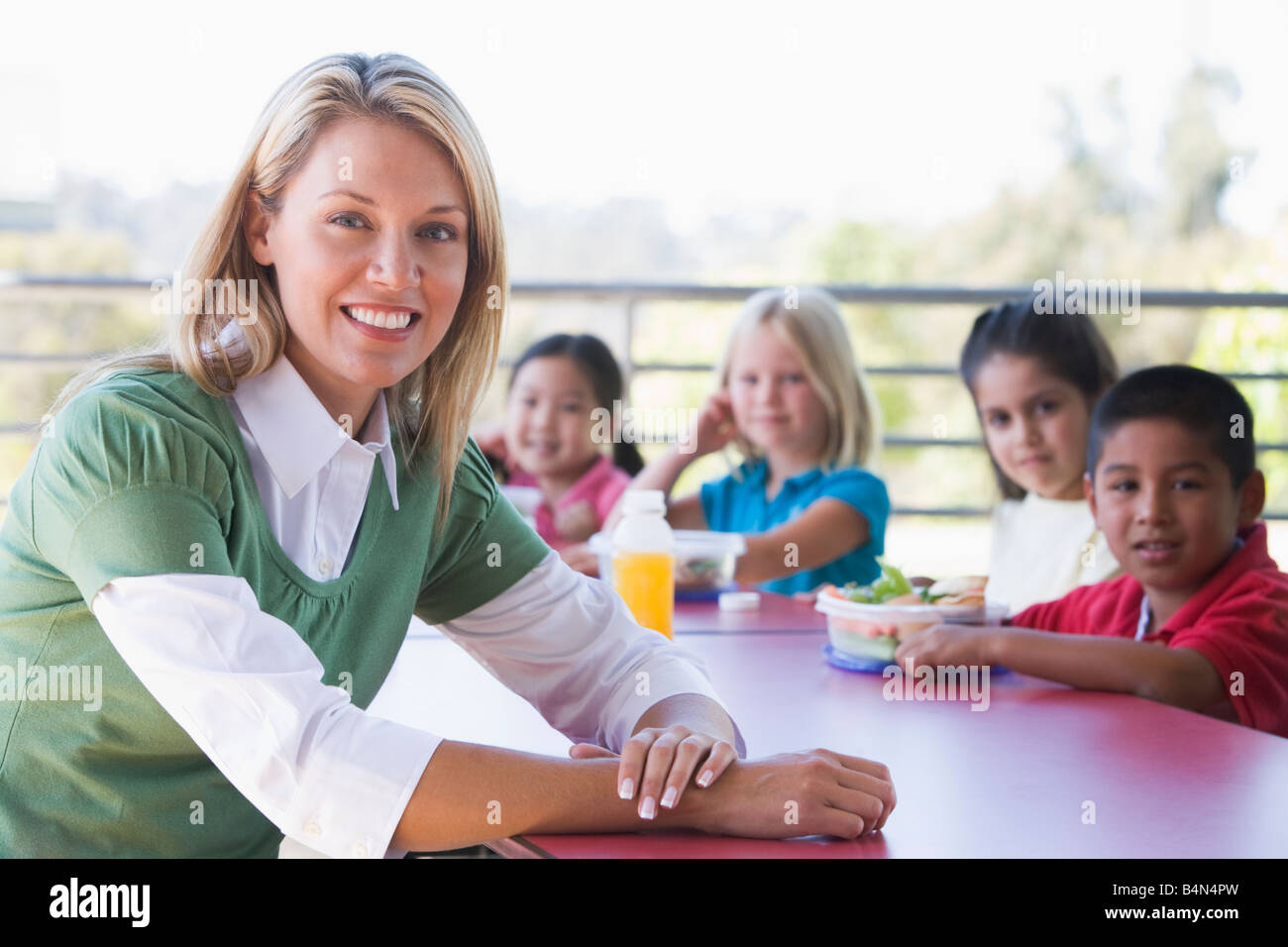Teacher sitting at table outdoors with students eating lunch in ...