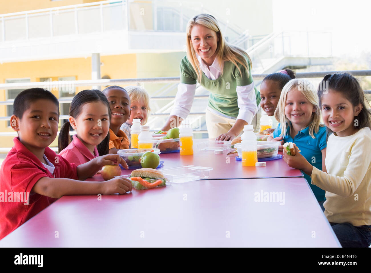Teacher leaning on table outdoors while students eat lunch (high key ...