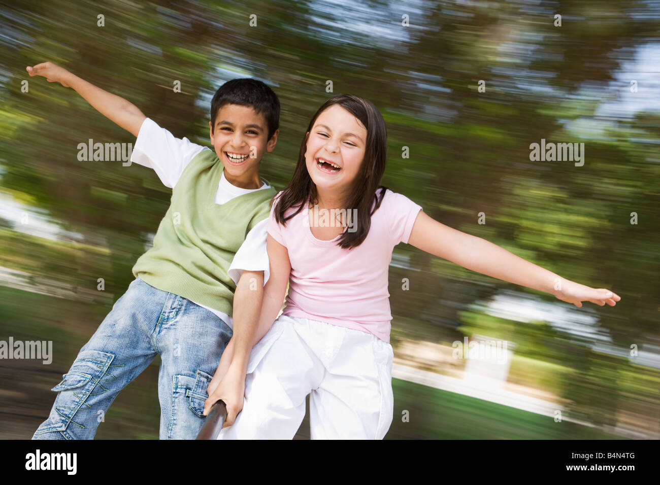 Two young children outdoors in playground spinning and smiling (blur ...