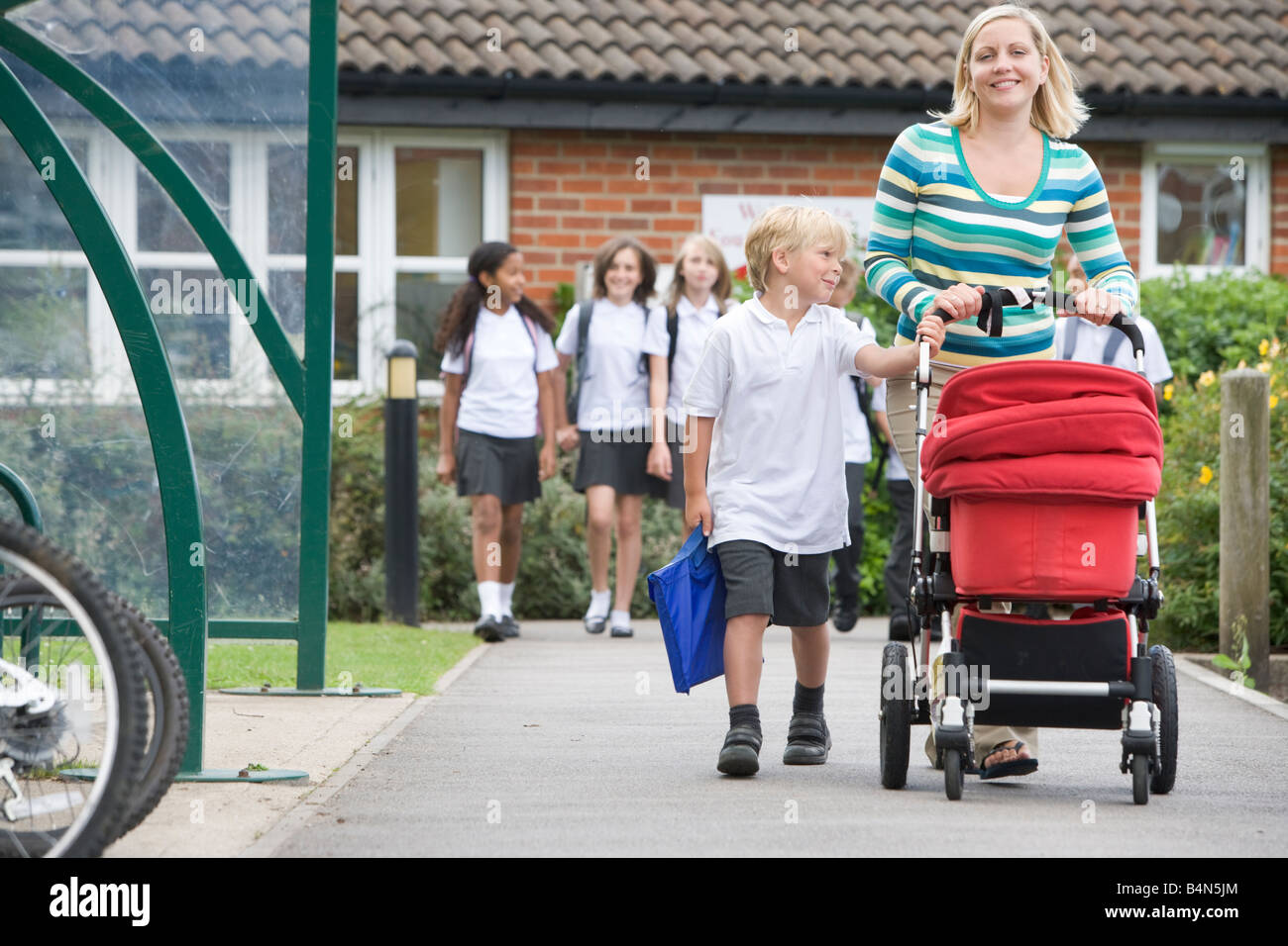 Woman and young boy pushing a stroller outside school with students in ...