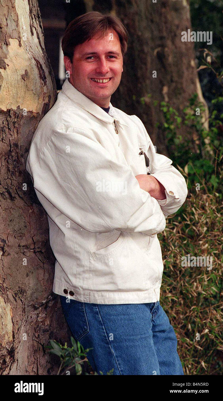 Actor Gary Webster leaning against tree arms folded white jacket and ...