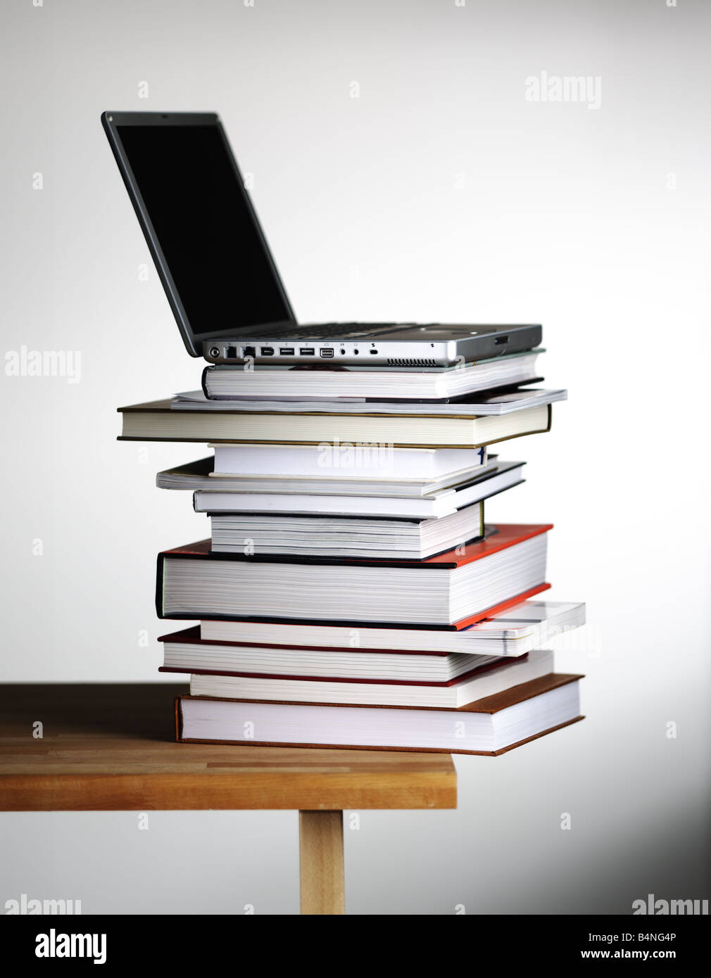 Open laptop computer on top of pile of books on table edge white ...