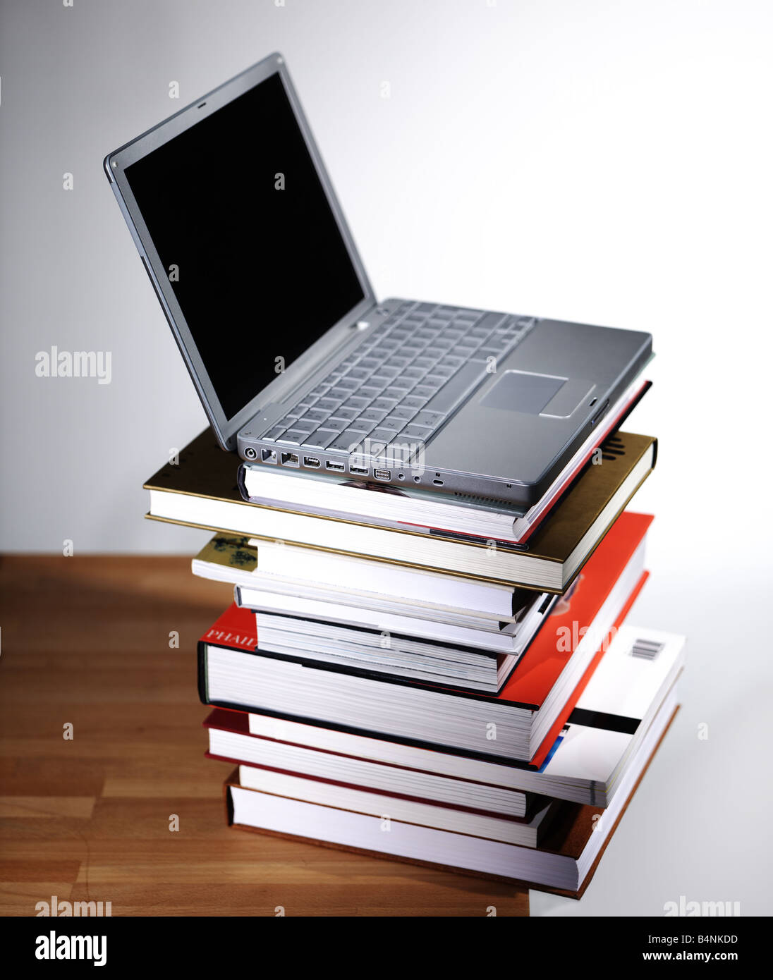 Open laptop computer on top of pile of books on table edge white ...