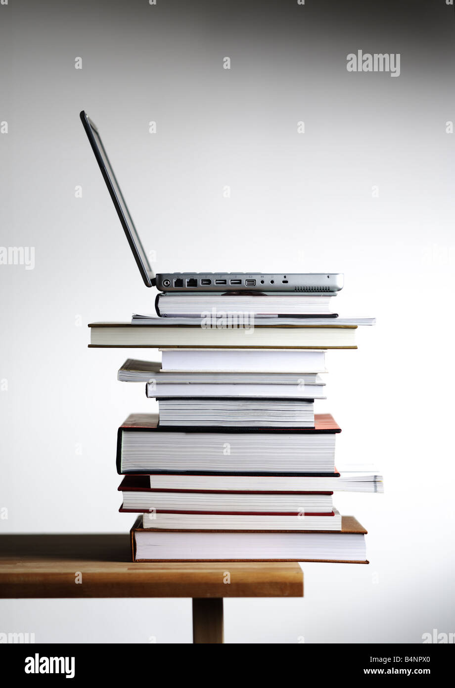 Open laptop computer on top of pile of books on table edge white ...