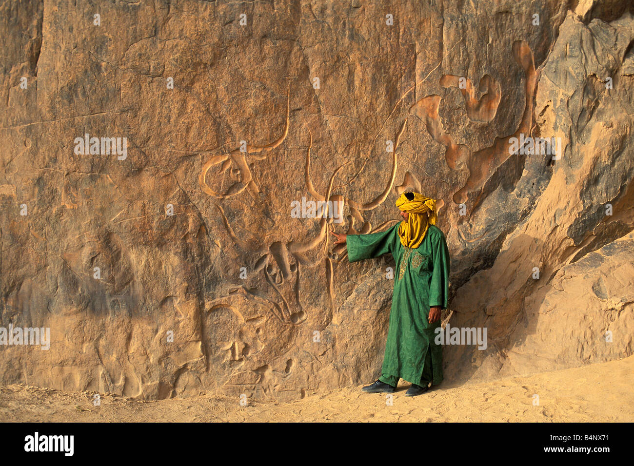 Algeria Djanet Man of Tuareg tribe in front of prehistoric engraving ...