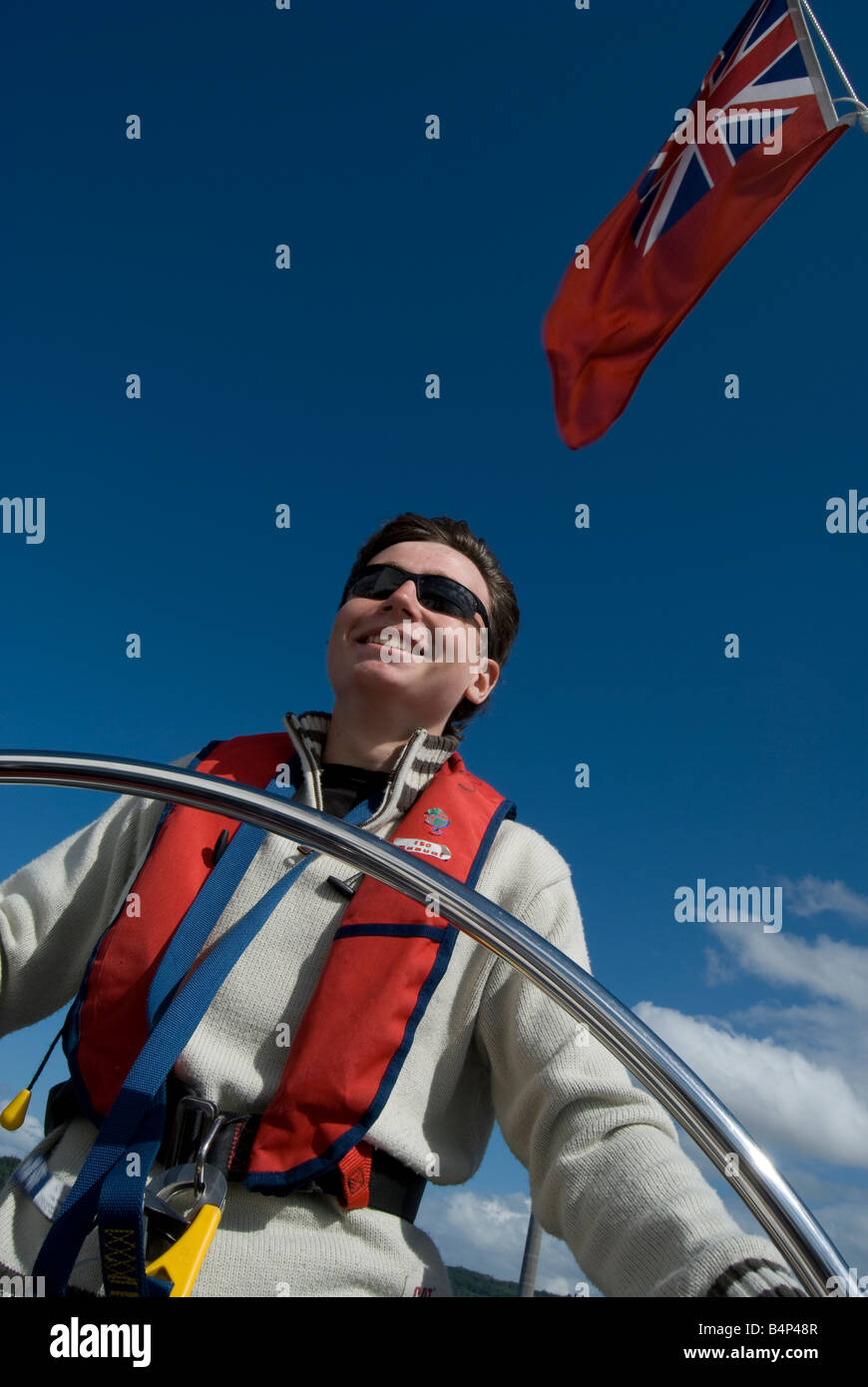 Young man helming a sailing yacht the Red Ensign fluttering in the ...