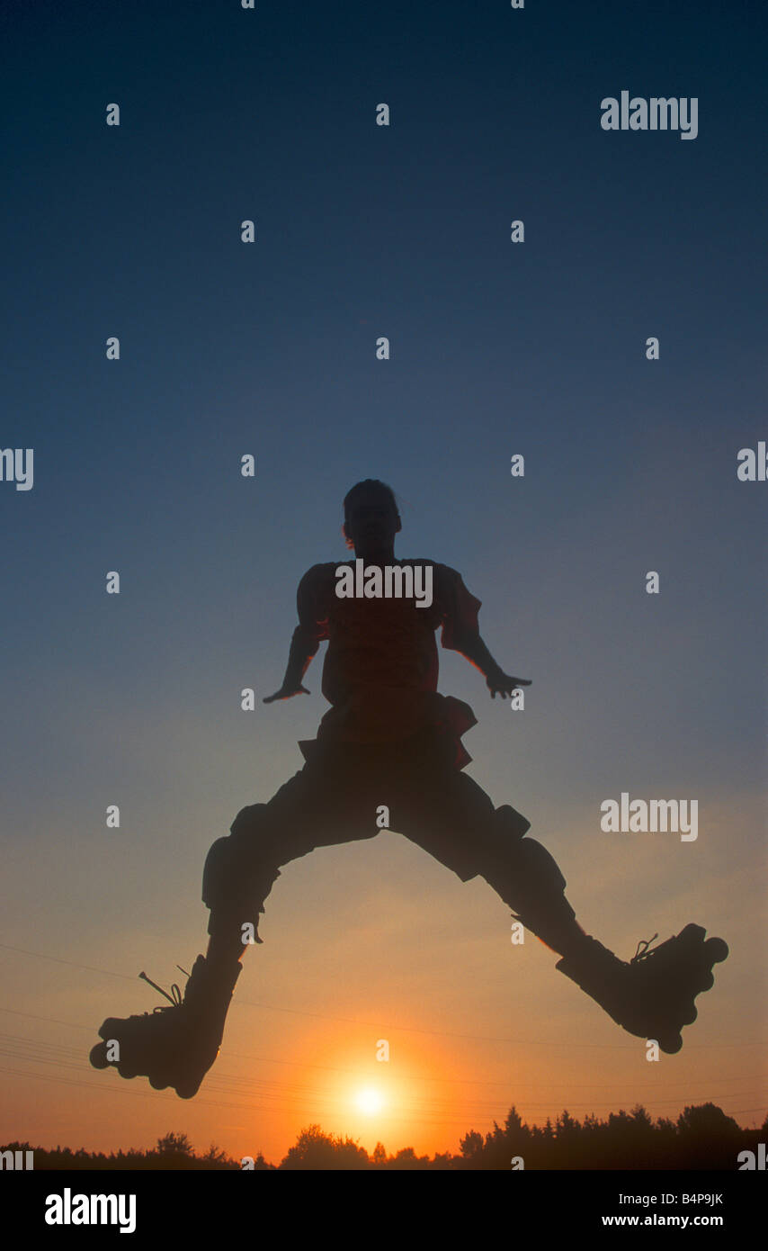 Teenage boy jumping with his in-line skates with the sun setting behind ...
