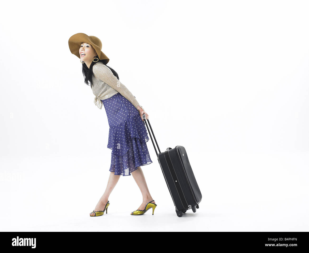 Young woman wearing hat and pulling suitcase Stock Photo - Alamy
