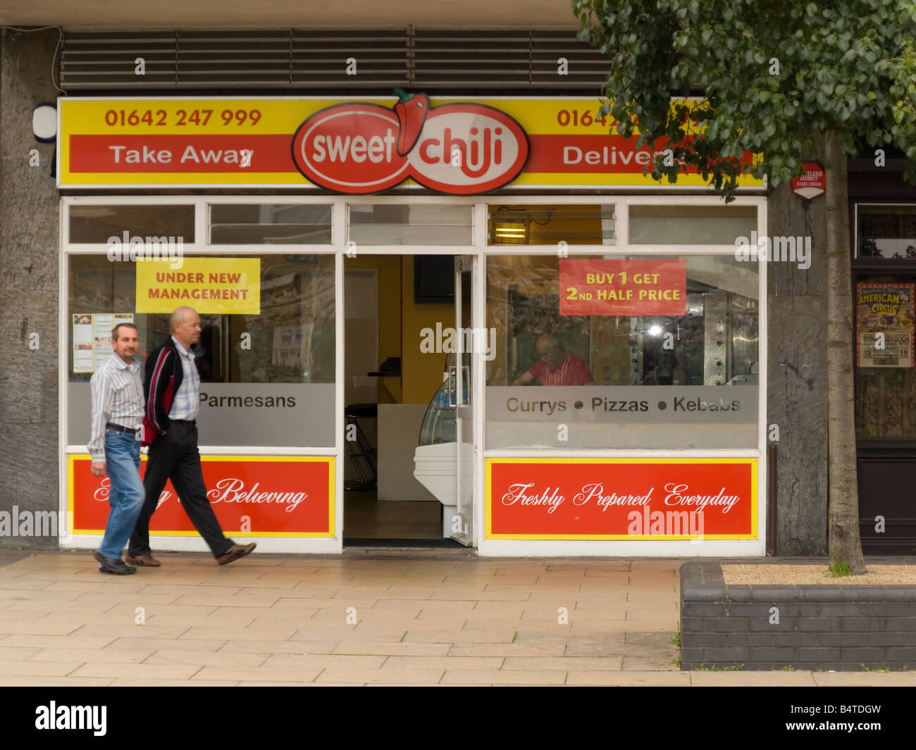 Two men walking past a brightly coloured take away food shop in ...