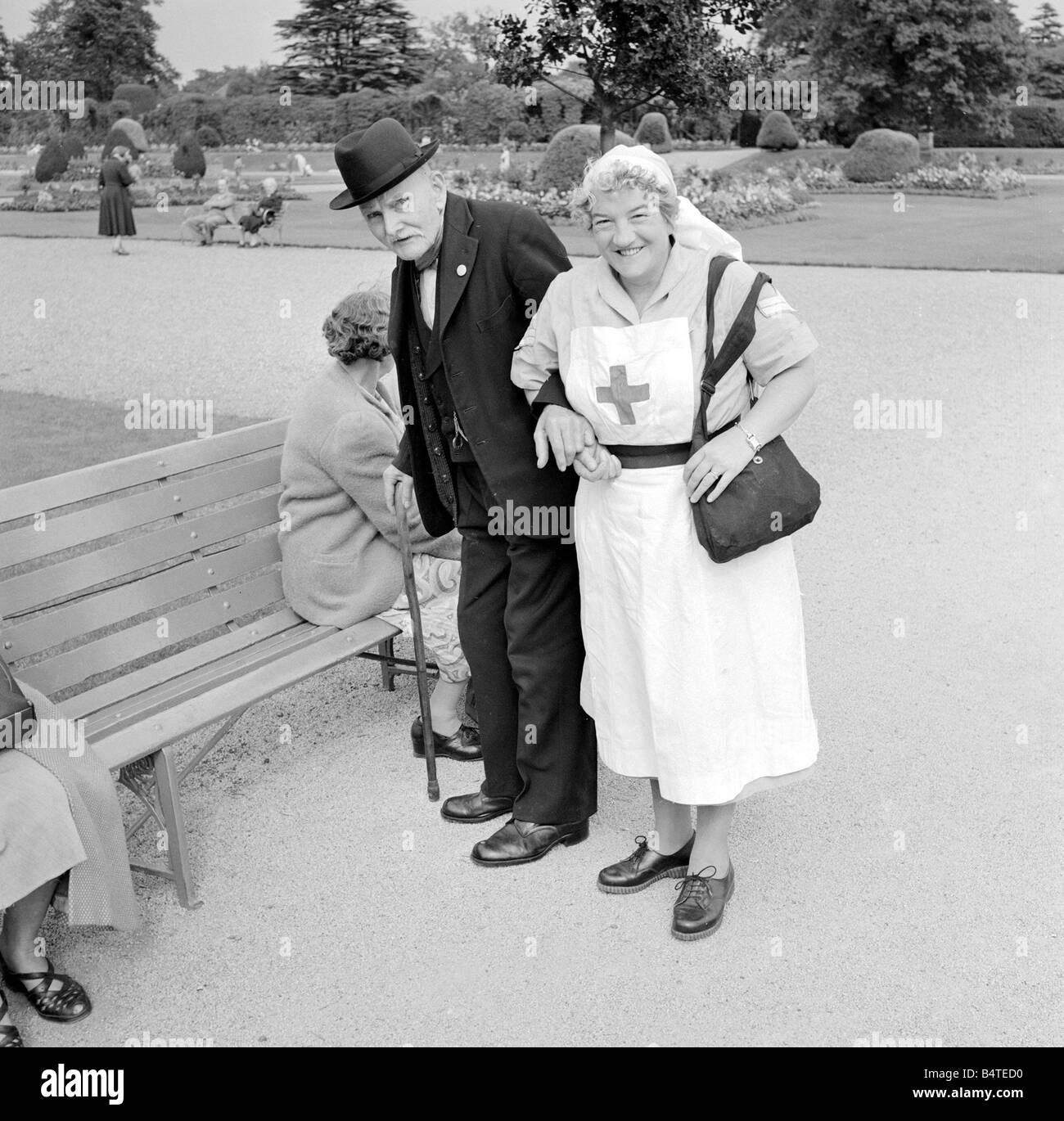 A Red Cross nurse helps and elderly gentleman to a bench during a day ...