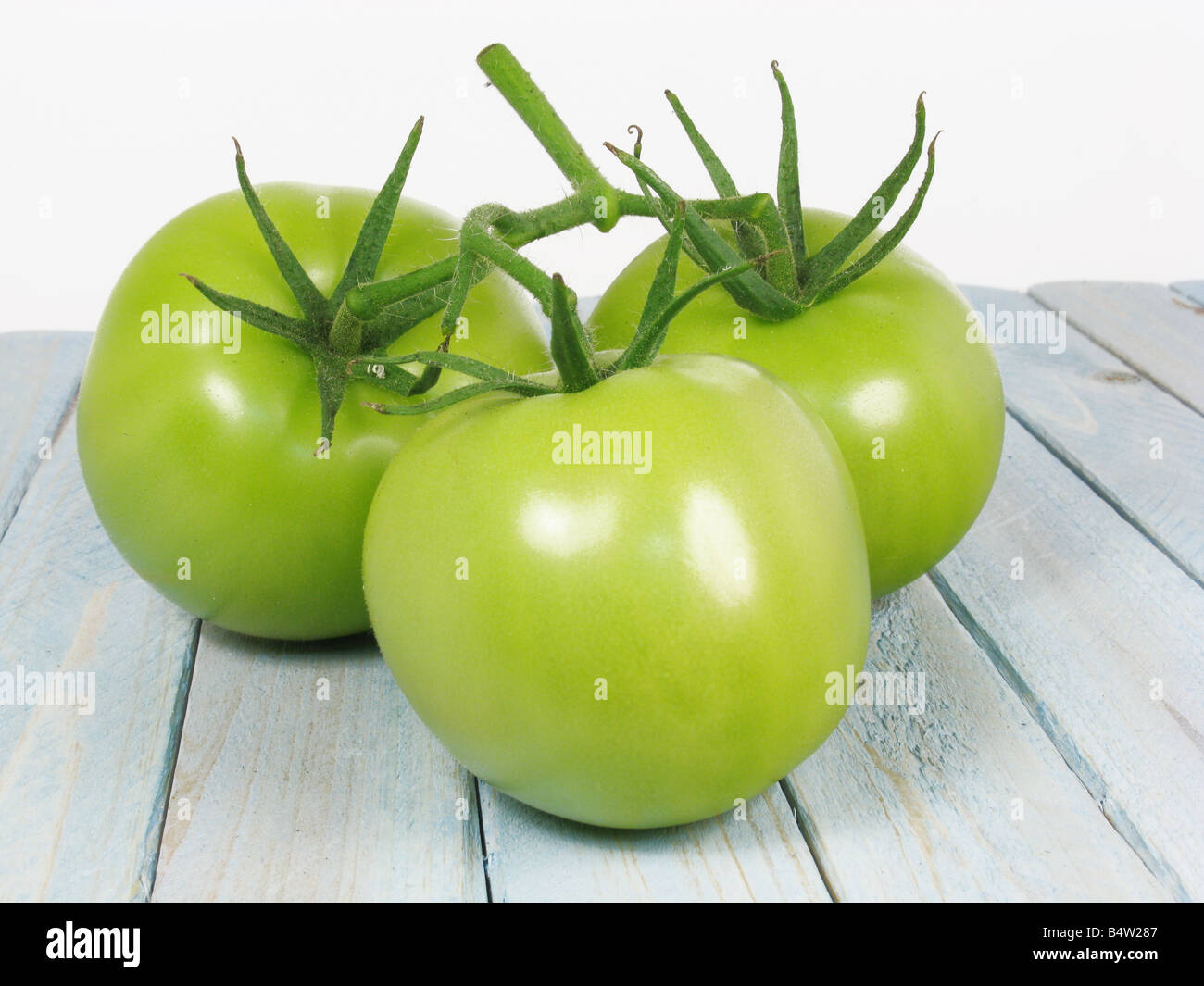 three unripe tomatoes on a wooden table Stock Photo - Alamy