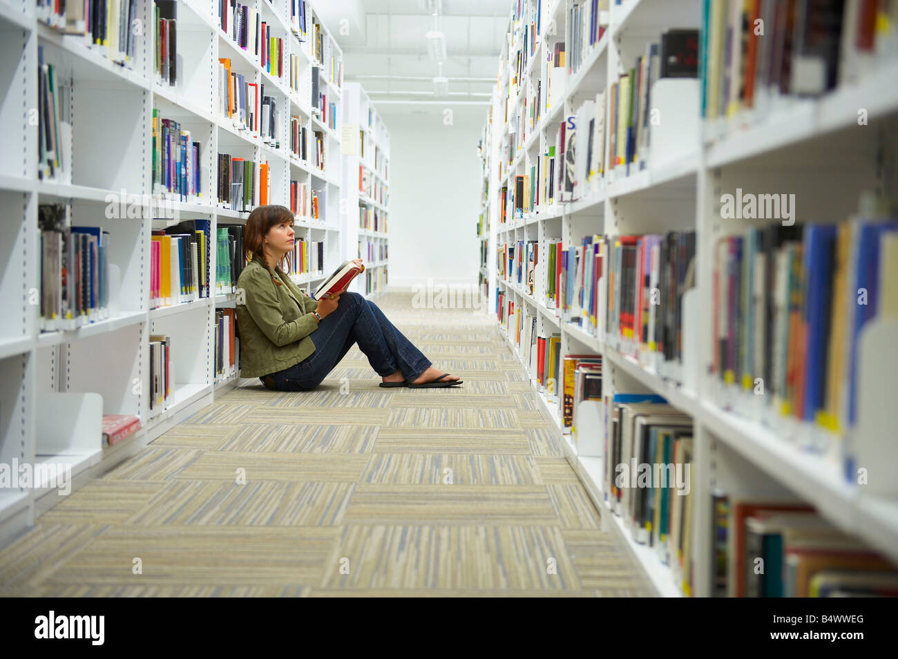 Young woman sitting on library floor Stock Photo - Alamy
