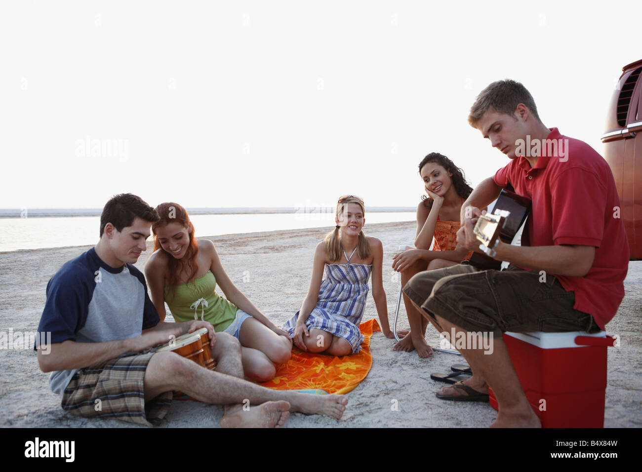Group of people sitting on beach with guitar at sunset hi-res stock ...