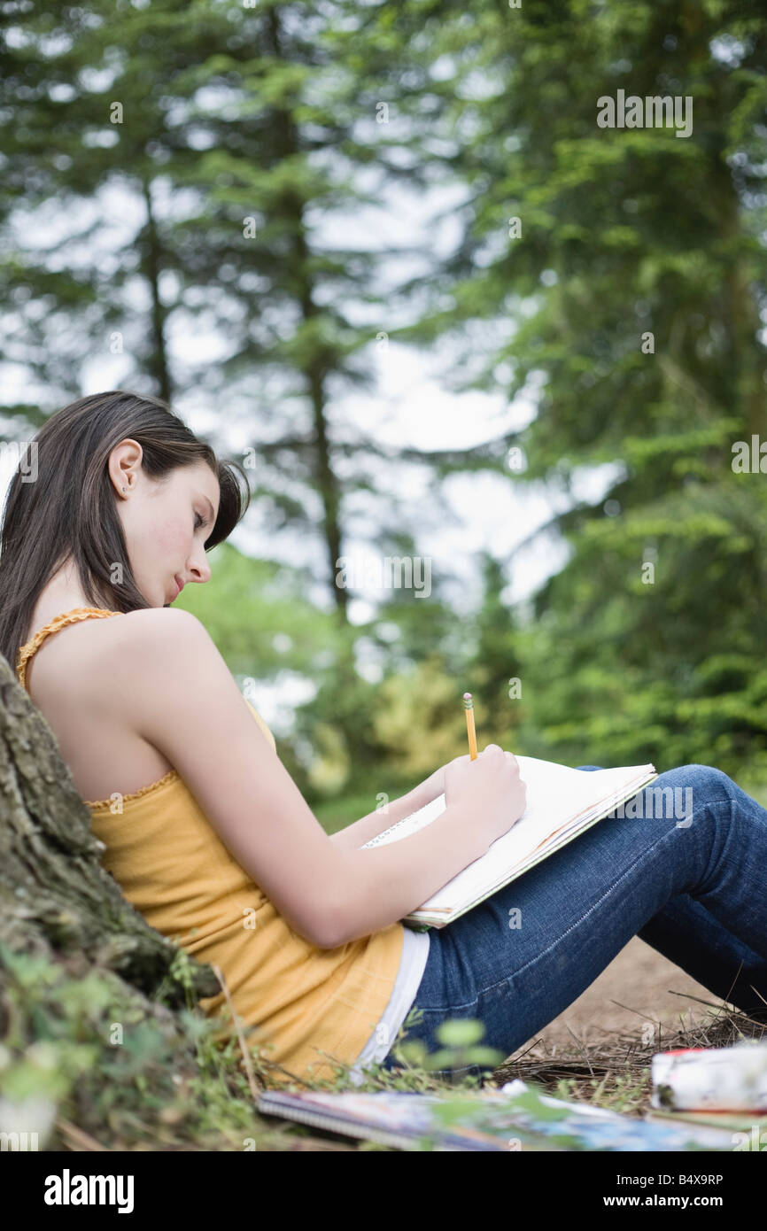 Girl leaning against tree writing in notebook Stock Photo - Alamy