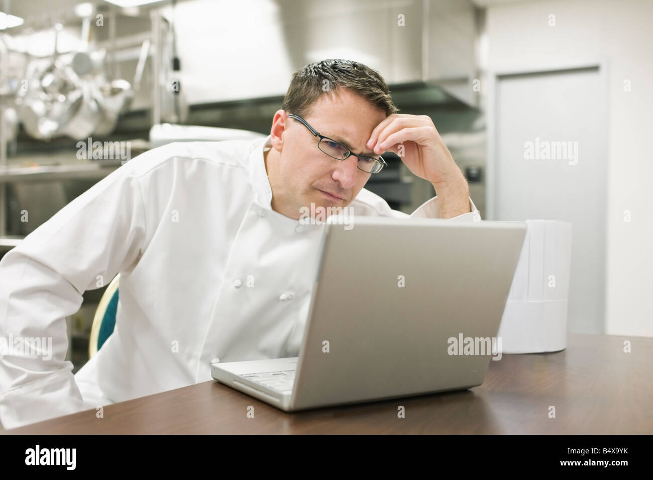 Frustrated chef looking at laptop in kitchen Stock Photo - Alamy