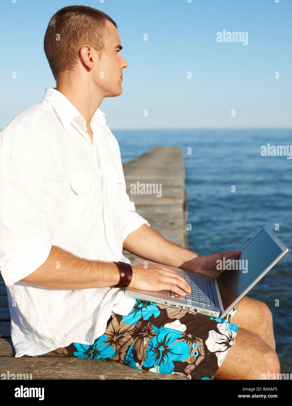Young man using laptop on dock Stock Photo - Alamy
