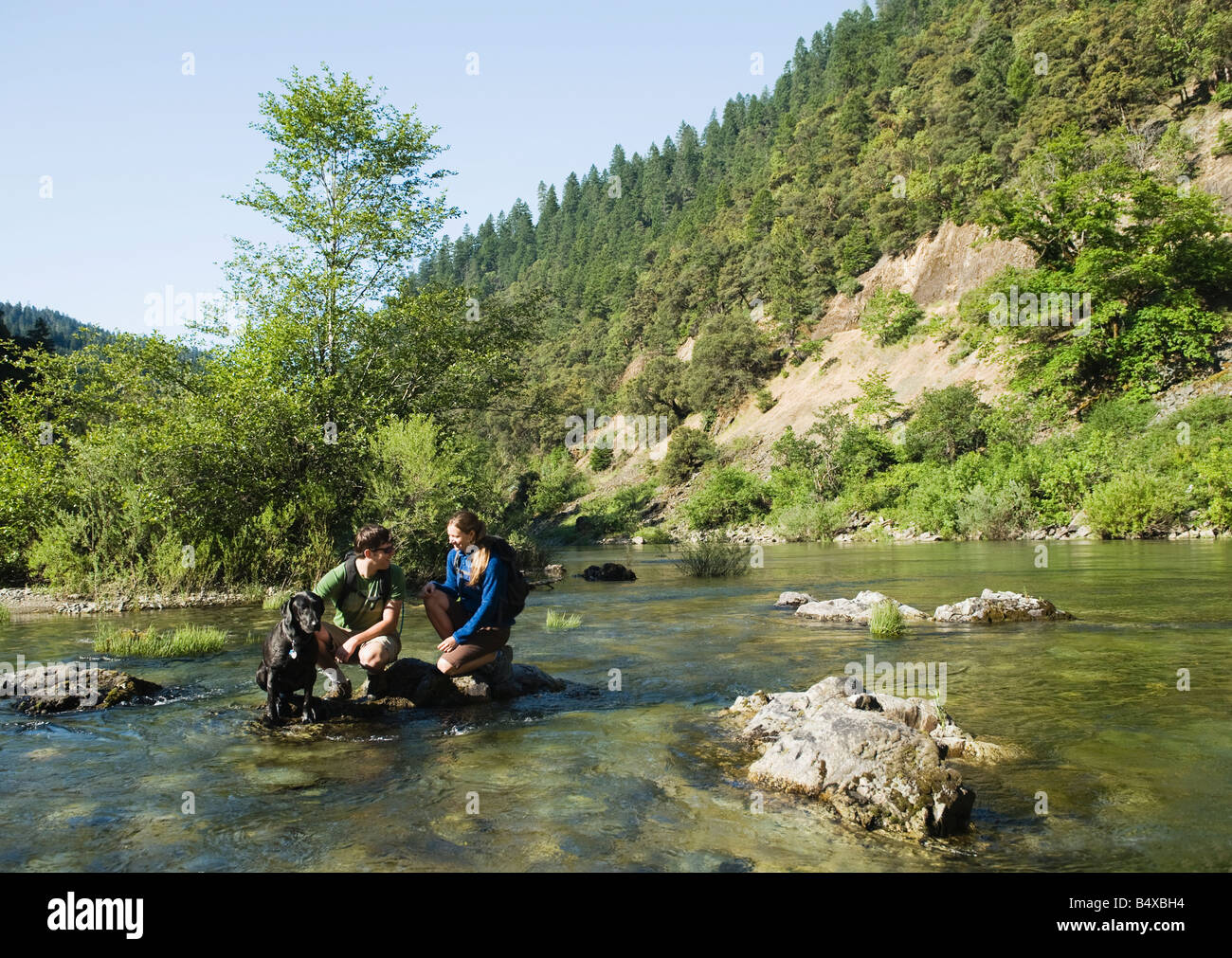 Hikers resting on rock in middle of river Stock Photo - Alamy