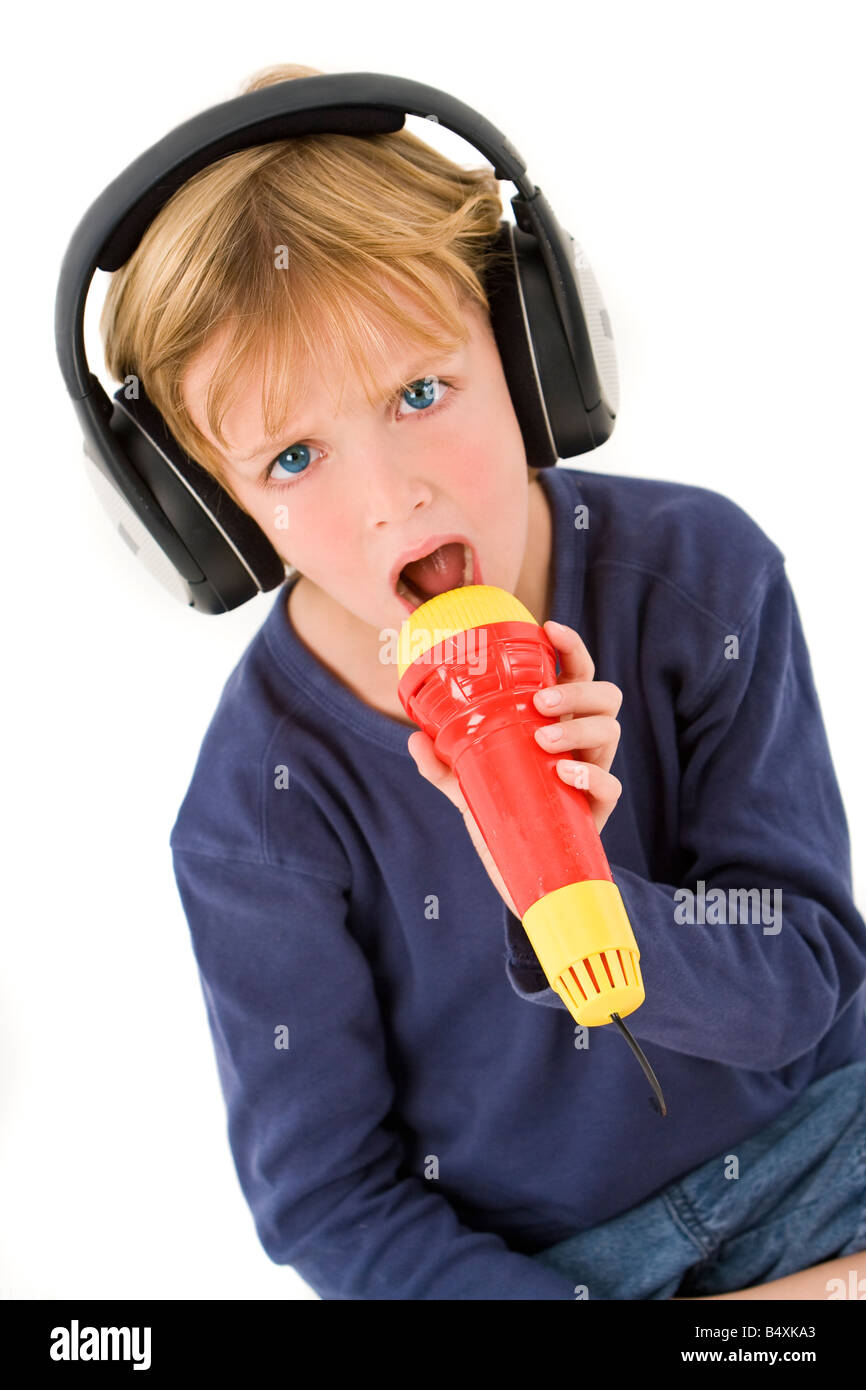 A young blond boy wearing headphones and singing into a toy microphone ...