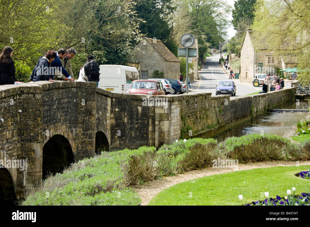 Tourists watching trout in the river Coln from a stone bridge in the ...