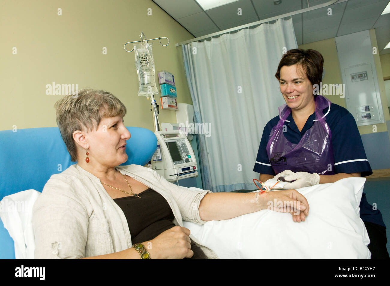 Nurse and cancer patient are smiling as chemotherapy drug is injected ...