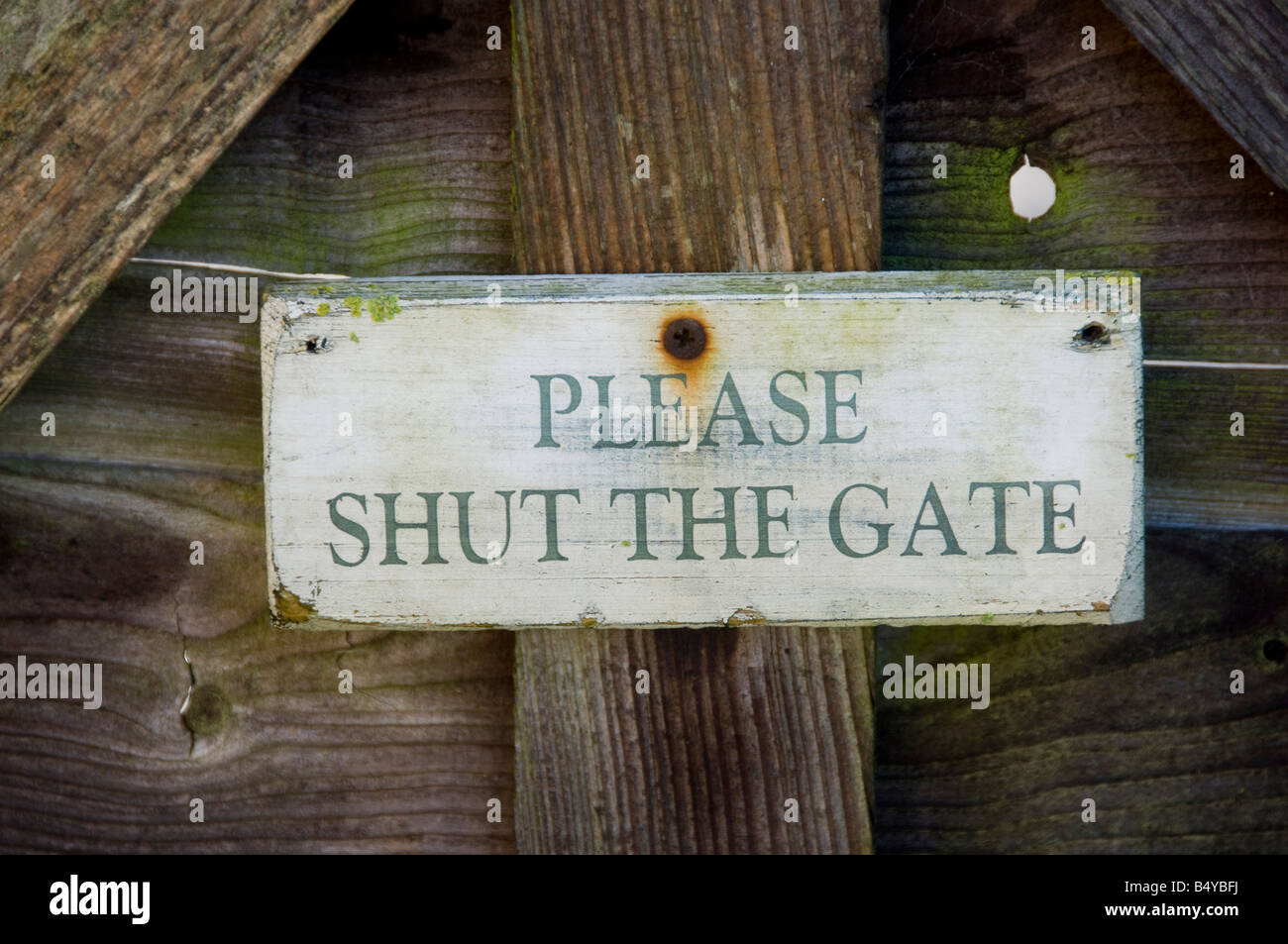 Wooden sign on a garden gate reading please shut the gate held on by a ...