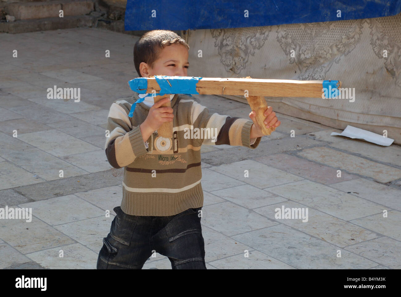 An Arab boy using a piece of wood as a toy gun in a cobbled courtyard ...