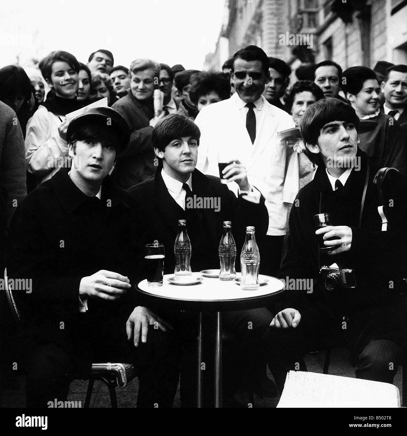 Beatles sitting round a small table with three bottles of Coca Cola all ...