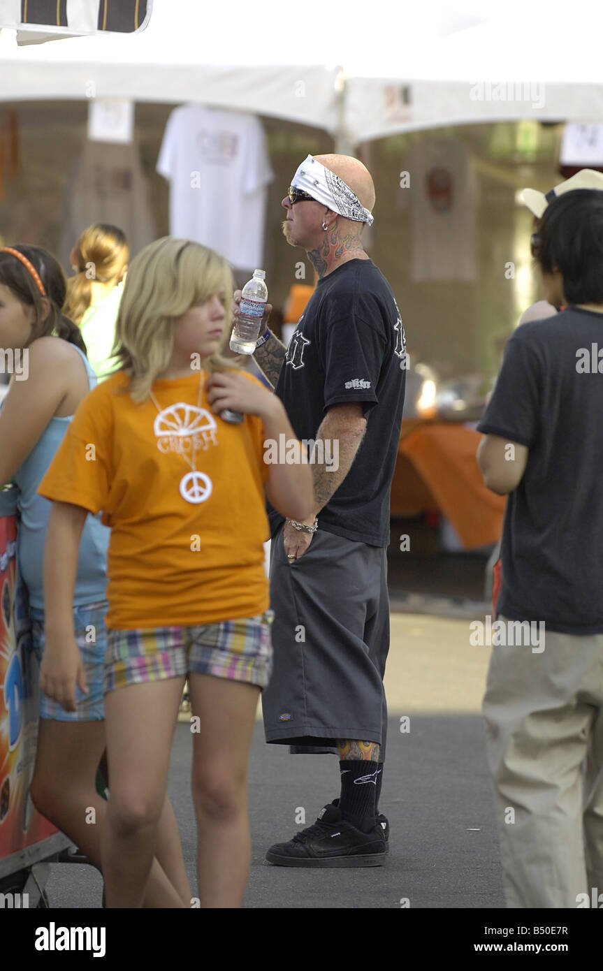 A man with tattoos bandanna and street gang attire stands drinking a ...
