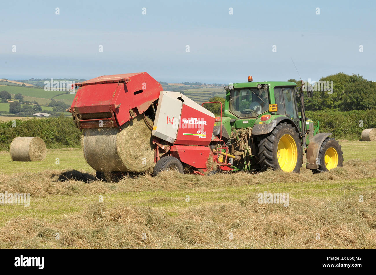 Tractor-towed baling machine disgorging its latest bundle of hay ...