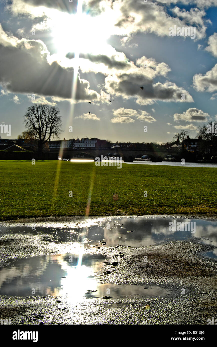 A starburst sun is reflected in the puddles on the ground giving an oil ...