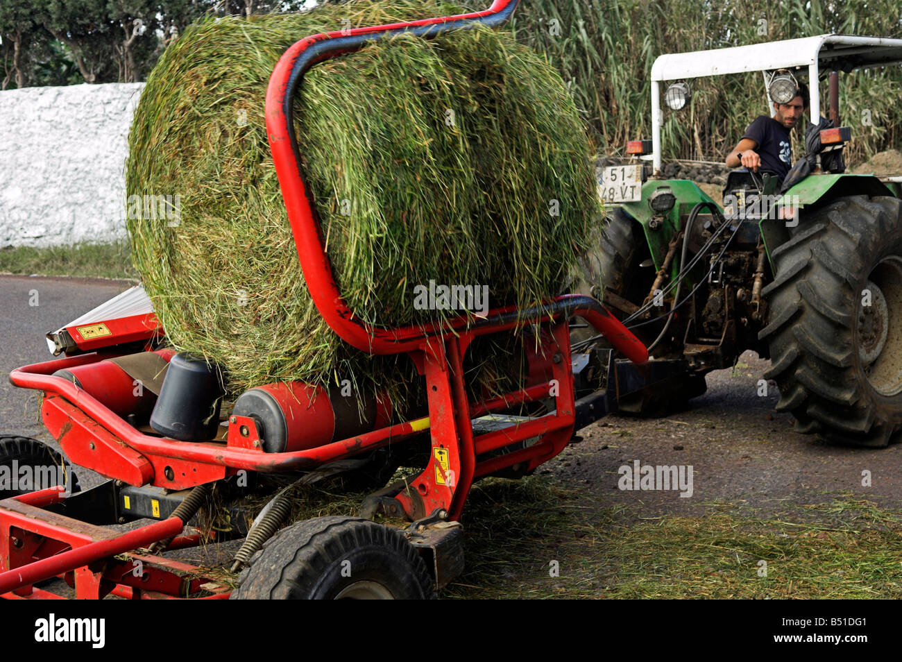 Tractor picking up round hay bail with autowrap machine Stock Photo - Alamy