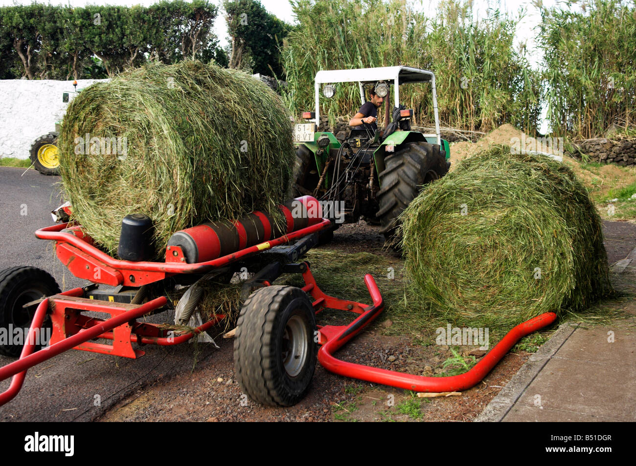 Tractor picking up round hay bail with autowrap machine Stock Photo - Alamy