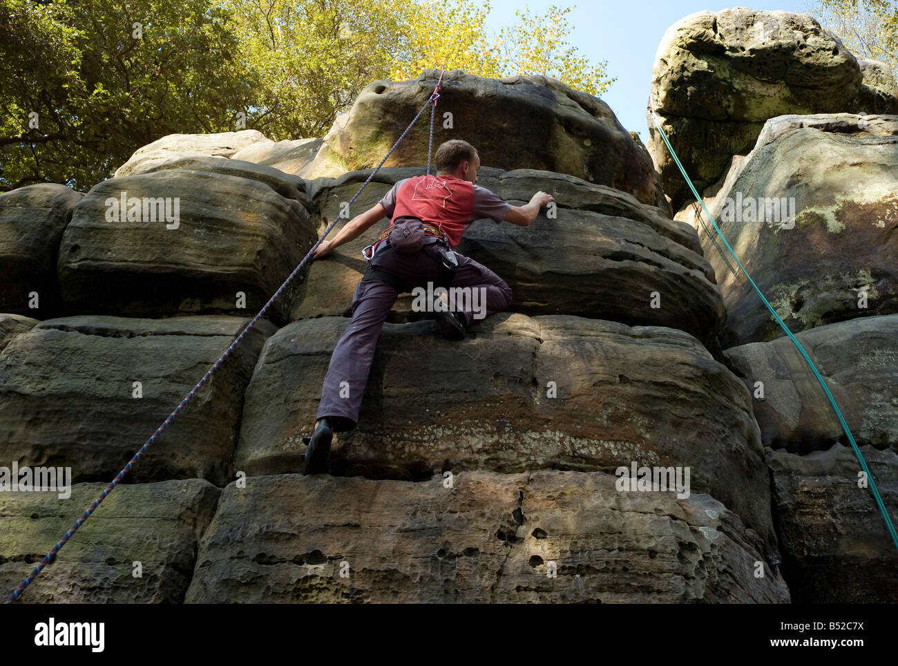 Young man climbing with ropes near top of sandstone crag, Harrisons ...