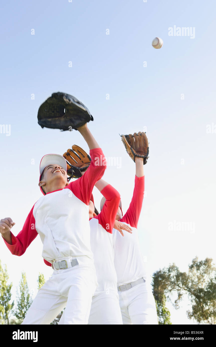 Multi-ethnic boys in baseball uniforms jumping to catch baseball Stock ...